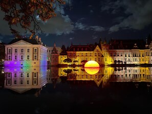 Um edifício histórico com arquitetura clássica, uma superfície aquática refletora e uma esfera grande iluminada.