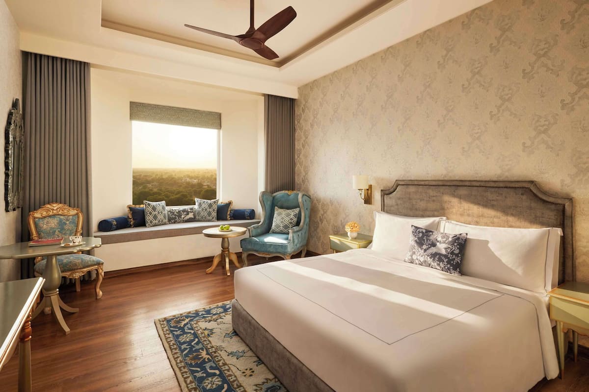 Quarto de hotel com uma cama grande, área de estar com uma cadeira e uma mesa, janela com vista e ventoinha no teto.