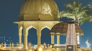 Vista noturna de um pavilhão tradicional com cúpula e arcos, cercado por mesas e cadeiras, provavelmente parte de um hotel ou resort.