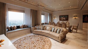 Uma sala de estar luxuosa com um amplo sofá bege, um tapete redondo estampado e vista para a cidade através de grandes janelas.