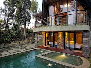 Uma casa moderna de dois andares com piscina, paredes de pedra e uma varanda com plantas.