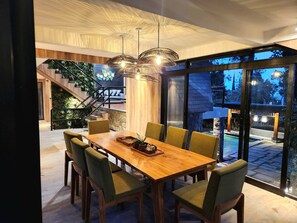 Uma sala de jantar moderna com mesa de madeira e cadeiras estofadas em verde, janelas amplas e escada com plantas.