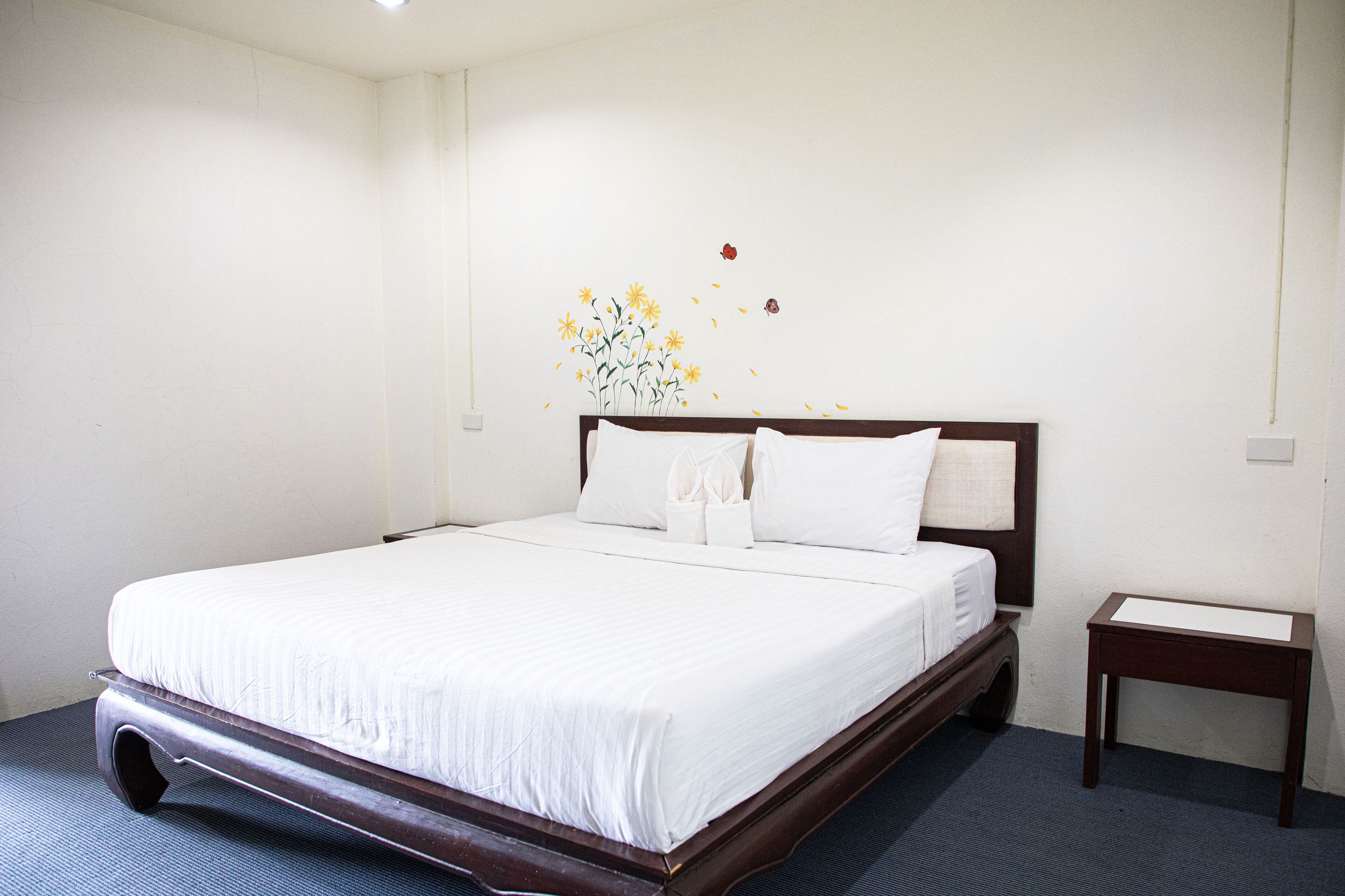 Cama bem arrumada com lençóis brancos, cabeceira de madeira e pequena mesa de cabeceira com abajur.