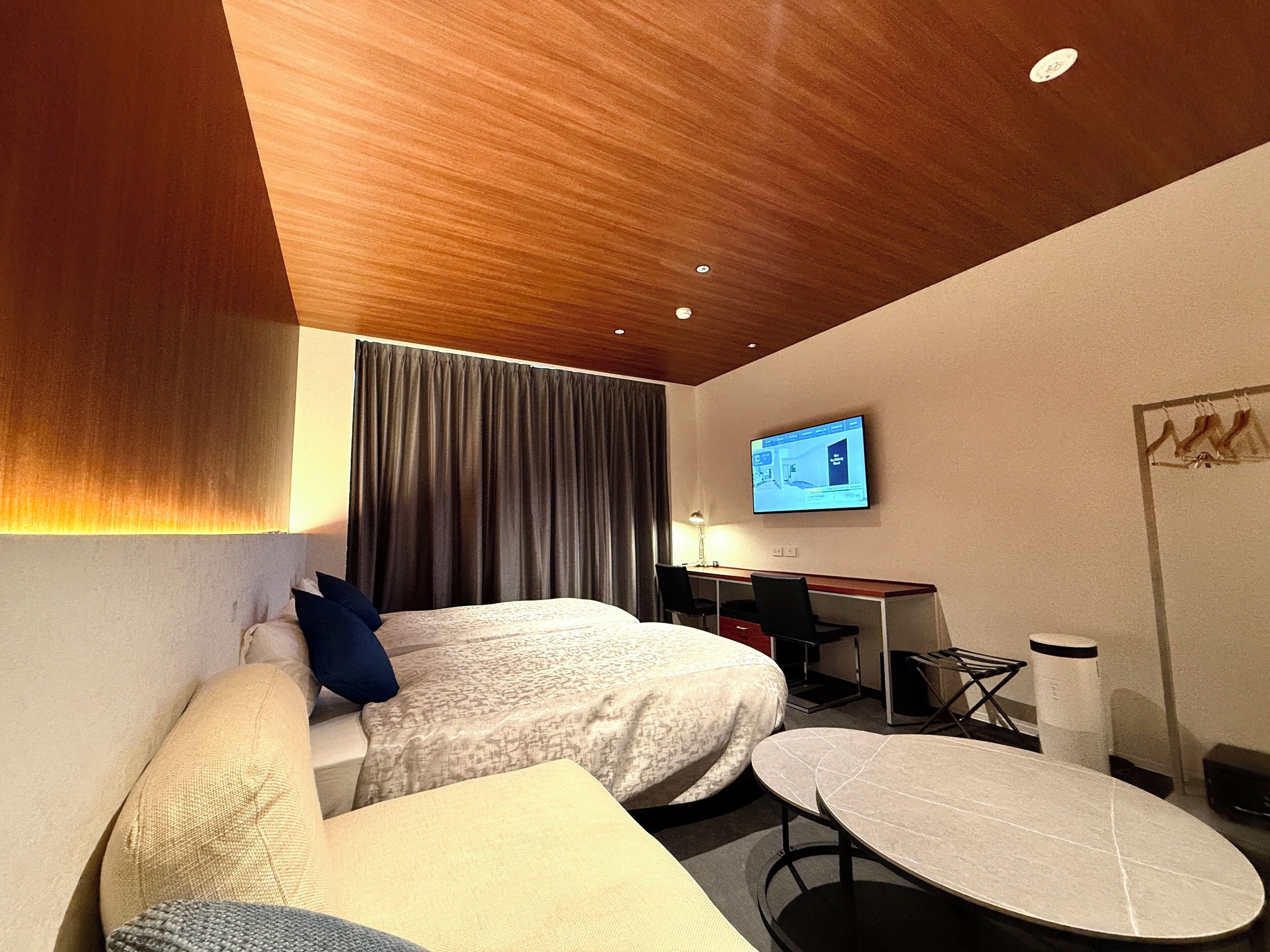 Quarto de hotel moderno com duas camas, uma escrivaninha, televisão e uma mesinha.
