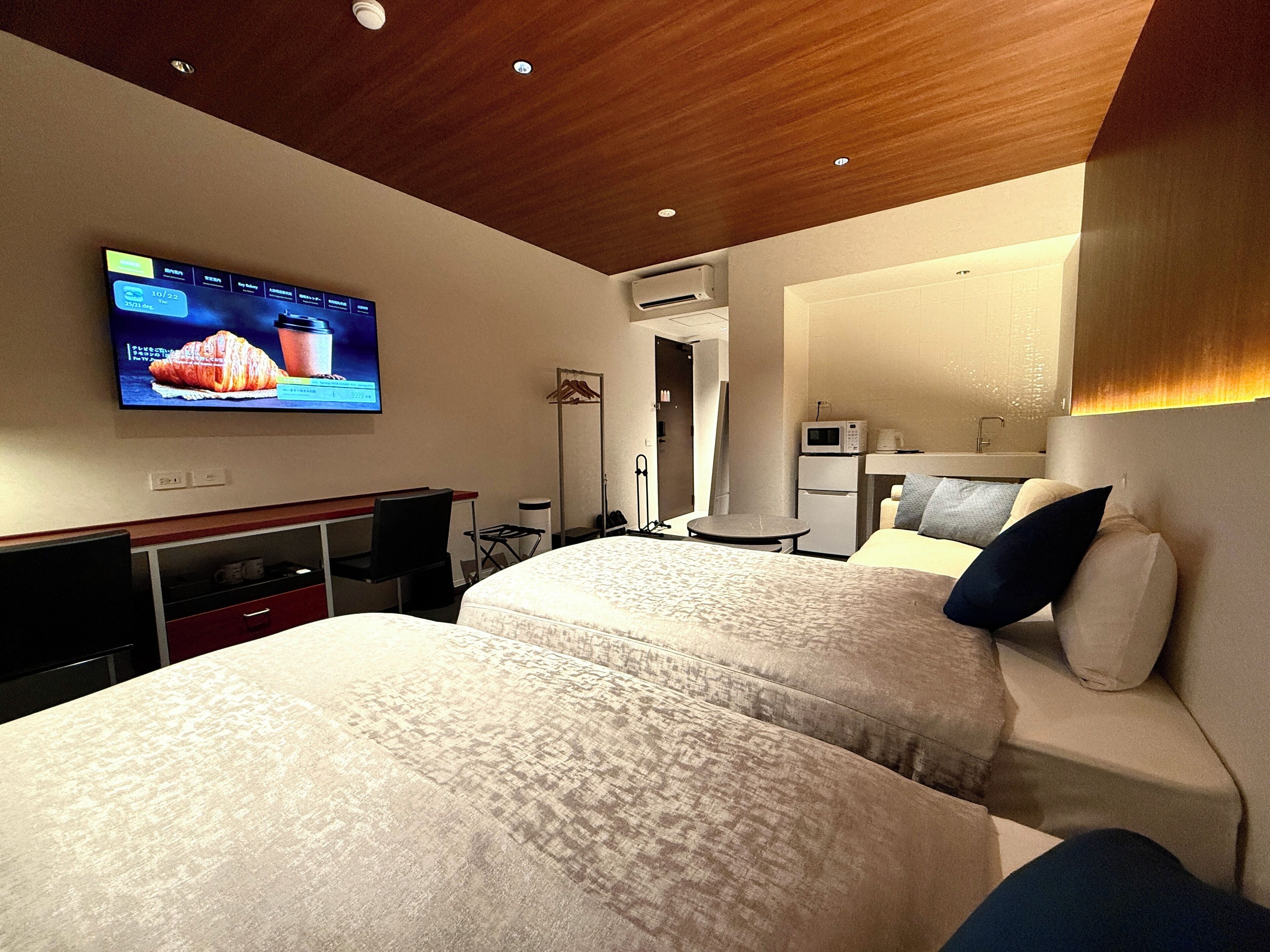 Quarto de hotel com duas camas, uma televisão na parede, uma escrivaninha e um guarda-roupa.