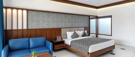 Quarto moderno com uma cama, um sofá azul, uma mesinha de cabeceira de madeira e uma janela grande.