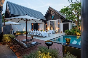 Uma área moderna para refeições ao ar livre, com mesas, cadeiras, piscina e um terraço bem iluminado.
