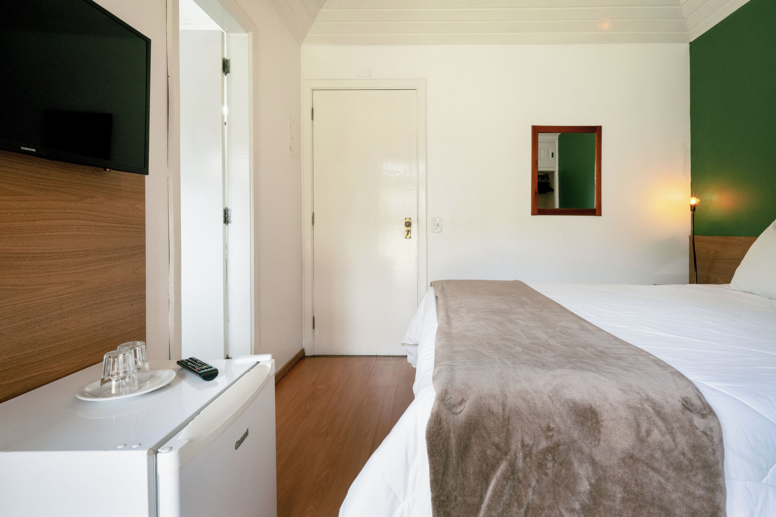 Quarto de hotel com cama, escrivaninha e televisão, além de espelho.