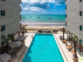 Uma área de piscina com vista para a praia e oceano, com espreguiçadeiras e guarda-sóis.