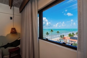 Quarto com vista para a praia, uma luminária e uma cadeira.