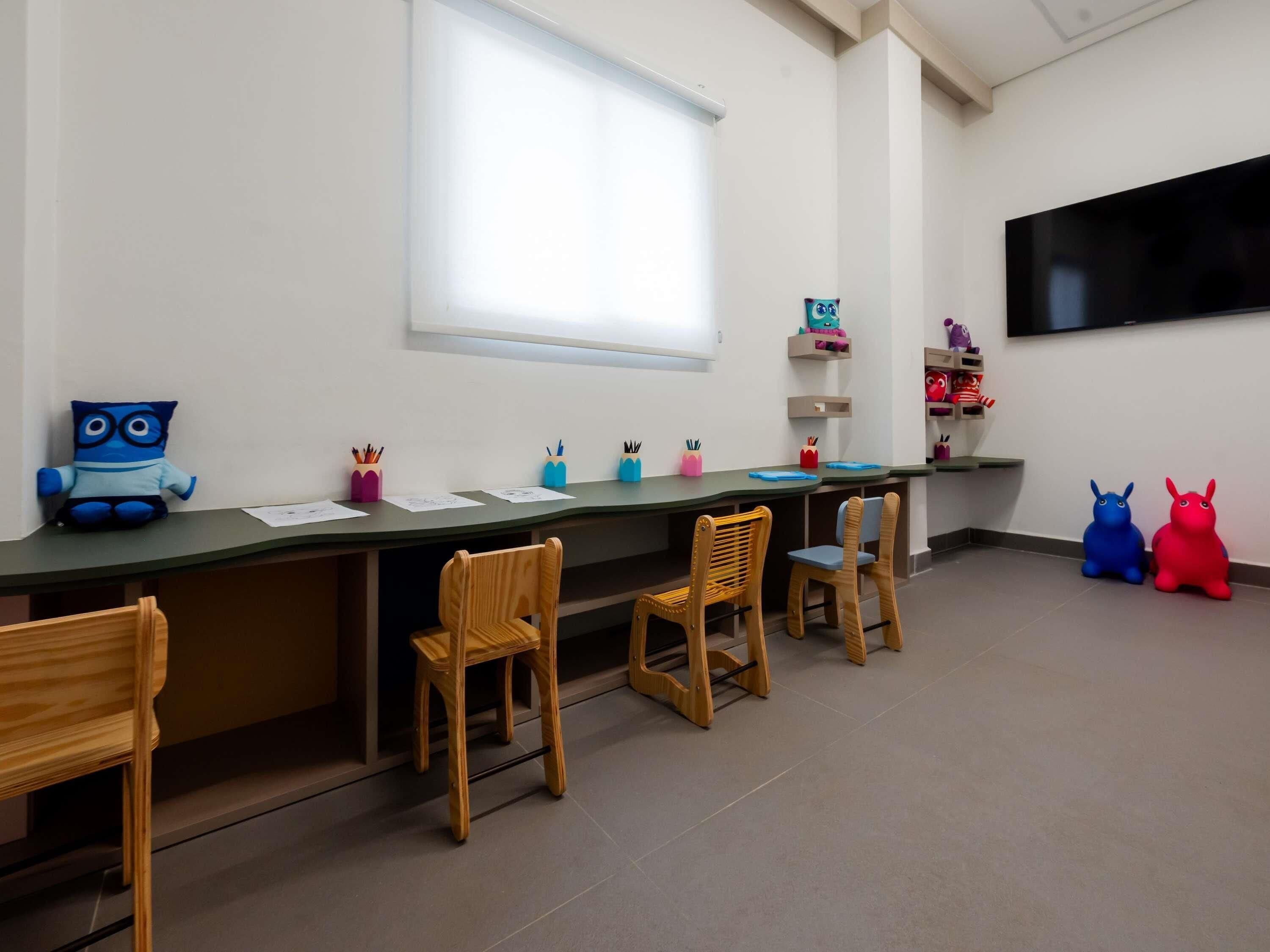 Uma sala de aula com uma mesa comprida, cadeiras e materiais educativos.