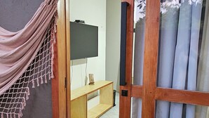 Um quarto com porta de madeira, rede, cama e televisão.