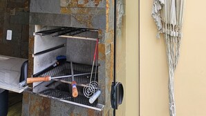 Uma churrasqueira ao ar livre de pedra com tampa de metal, cabo de madeira e uma grelha metálica.