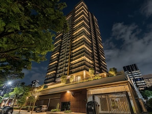 Um edifício alto com várias varandas, entrada com portão e área de estacionamento.