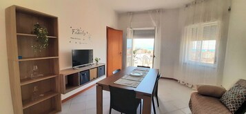 Espaço compacto com área de refeições, TV sobre uma estante de madeira, varanda com vista e um espaço de estar aconchegante.