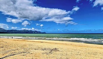 Uma praia com céu limpo e montanhas ao fundo.