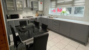 Uma cozinha moderna com armários cinza, uma mesa de jantar com cadeiras, um micro-ondas e uma janela com persianas.