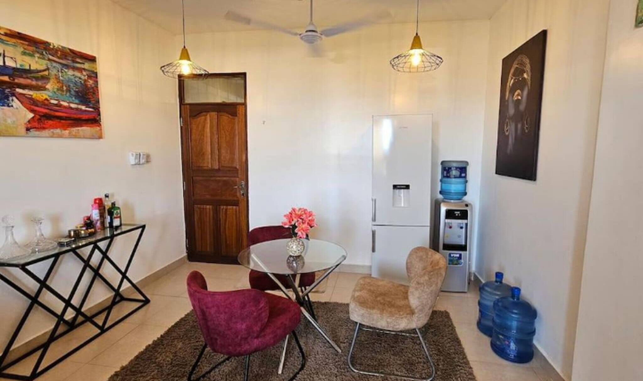 Um espaço compacto com mesa de jantar, duas cadeiras, geladeira e bebedouro.