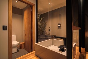 Um banheiro moderno com porta de madeira, vaso sanitário branco, uma banheira grande e box de vidro.