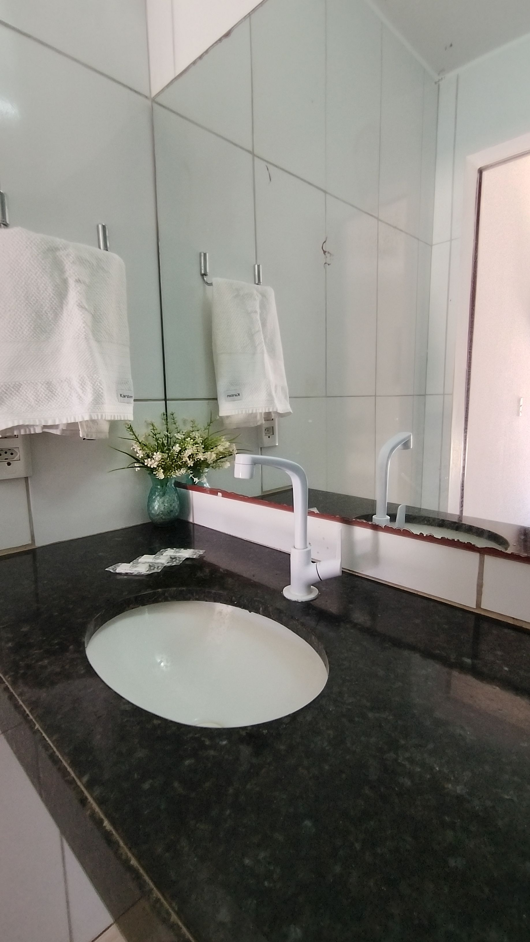 Casa de banho com lavatório branco, espelho e duas toalhas penduradas.