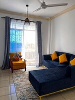 Uma sala de estar com um sofá azul, uma poltrona amarela e um ventilador de teto.
