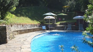 Piscina com degraus de pedra que descem até a água, rodeada por espreguiçadeiras e guarda-sóis.