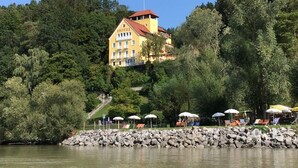 Hotel com telhado vermelho, rodeado por árvores e costa rochosa.