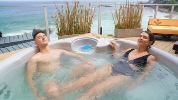 Um casal em uma banheira de hidromassagem com vista para o oceano.