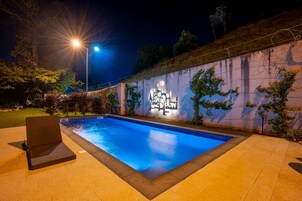 Piscina com área de estar rebaixada e parede com detalhes arquitetônicos iluminados.