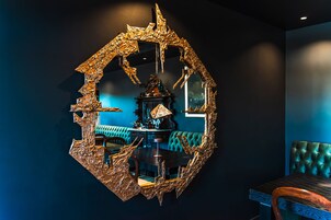 Um quarto com uma grande obra de arte circular em metal, um sofá verde com textura e uma mesa de madeira com tampo de vidro.