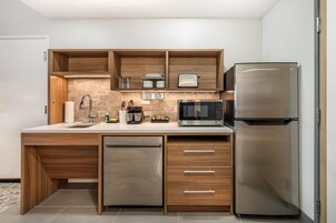 Uma cozinha compacta com máquina de lavar louça embutida, geladeira de aço inoxidável, micro-ondas e armários de madeira.