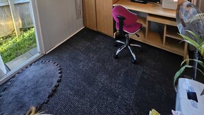 Quarto compacto com escrivaninha, cadeira, televisão e um pequeno ventilador.