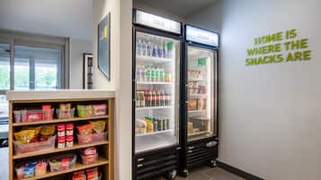Espaço de distribuição de lanches com freezer e prateleiras cheias de petiscos e bebidas.