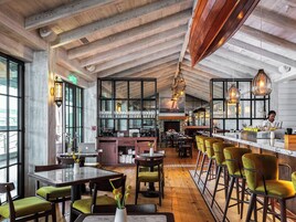 Um restaurante com tetos altos, vigas aparentes e um espaço de bar com banquetas.