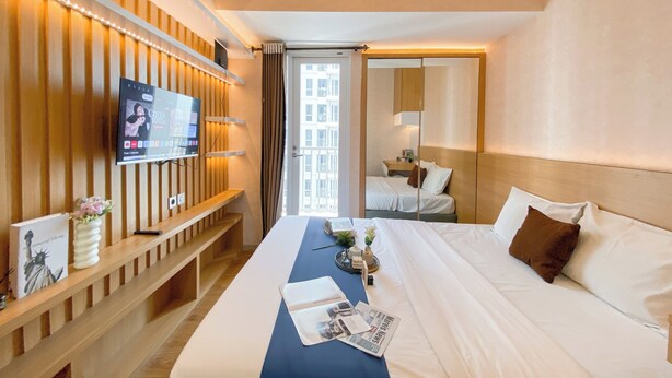 Quarto de hotel com uma cama grande, televisão na parede, escrivaninha com cadeira e janela com vista para edifícios.