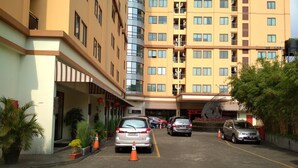 Entrada de hotel com vários carros estacionados em um acesso, cercada por plantas em vasos e cones de trânsito laranja.