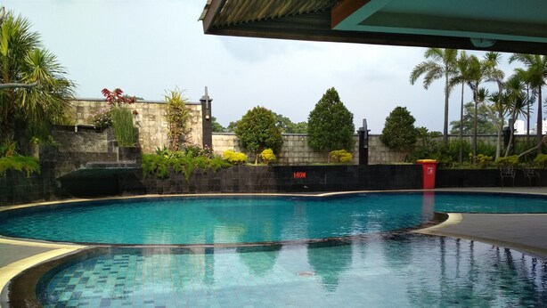 Piscina com borda azulejada, cercada por um muro de pedra e vegetação.