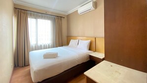 Quarto de hotel com cama, mesa de cabeceira, ar condicionado e janela com cortinas.