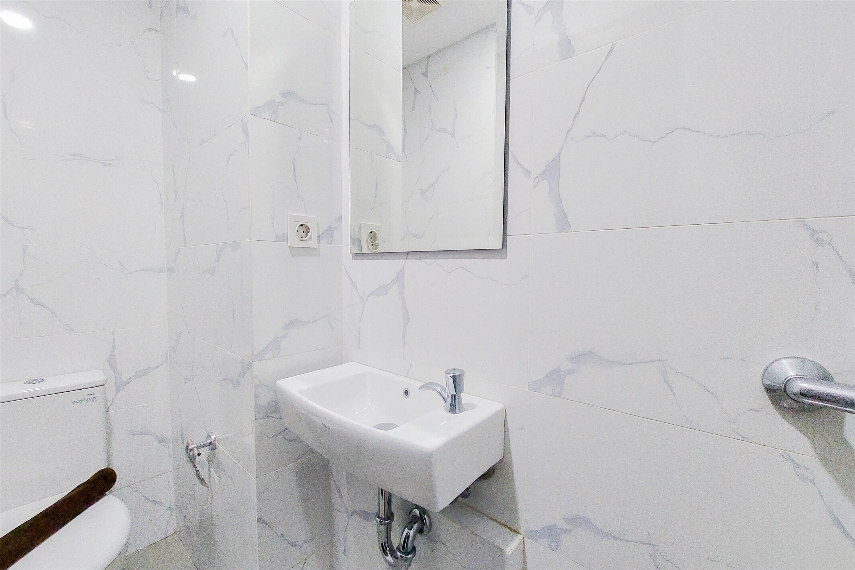Um banheiro com azulejos de mármore branco, pia branca, espelho e vaso sanitário.
