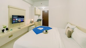 Quarto de hotel com uma cama, televisão na parede, escrivaninha com computador e pia pequena.