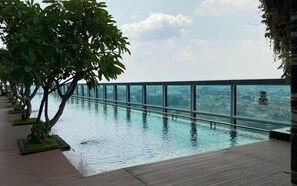 Piscina infinita no terraço, com barreira de vidro, rodeada por árvores e um deck de madeira.