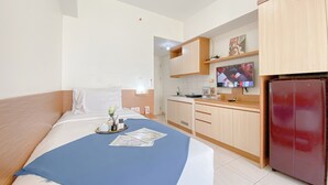 Quarto de hotel com cama, cozinha compacta, televisão e frigorífico.