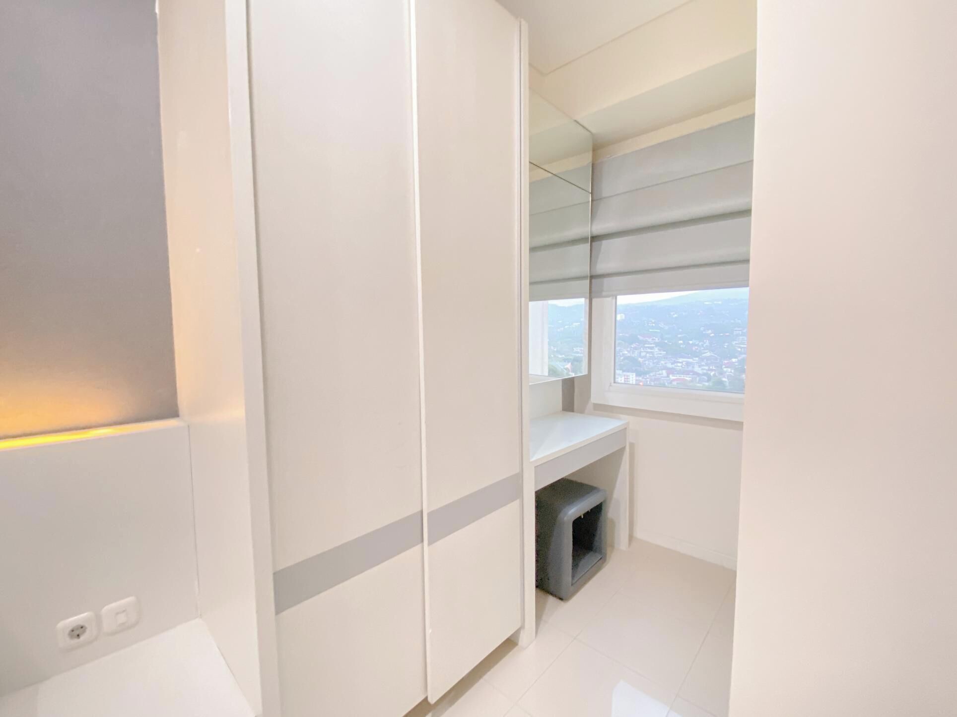 Quarto moderno e minimalista com uma janela grande que oferece vista para a cidade, um banco embutido e uma caminha pequena para animais de estimação.