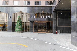 Entrada moderna de hotel com uma grande porta de vidro, uma árvore de Natal e uma placa com a inscrição "HOTEL ELORA".