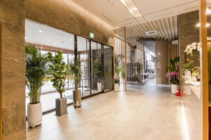Um hall amplo com design moderno, apresentando uma parede de vidro, plantas em vasos e um painel de madeira.