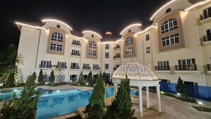 Um hotel de vários andares com piscina, um gazebo e uma lua crescente no céu.