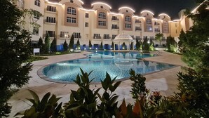 Um hotel com uma grande piscina ao ar livre, rodeado por jardins bem cuidados e um edifício de vários andares com varandas.