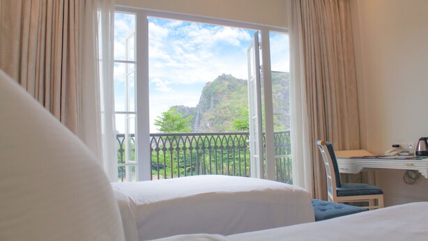 Quarto de hotel com duas camas, uma escrivaninha com cadeira e uma varanda com vista para uma paisagem montanhosa.
