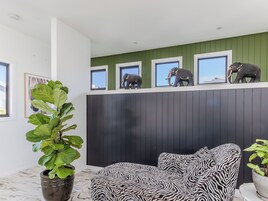 Uma sala de estar moderna com um sofá estampado com padrão de zebra, uma planta grande em vaso e esculturas de elefantes decorativas numa estante.