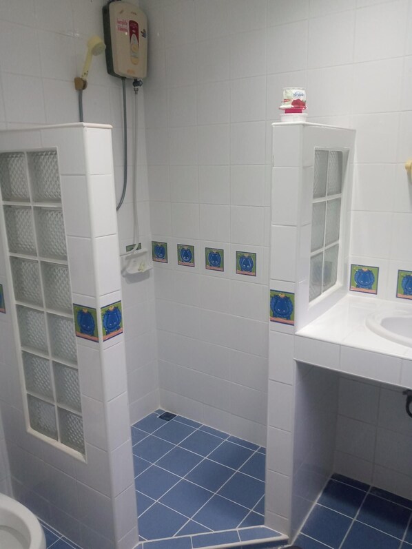 Uma casa de banho com paredes revestidas de azulejos brancos, chão em azulejos azuis, lavatório branco e cabine de duche.